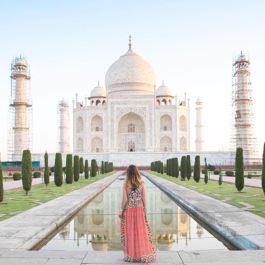 A woman standing by the water with the Taj Mahal in the background
