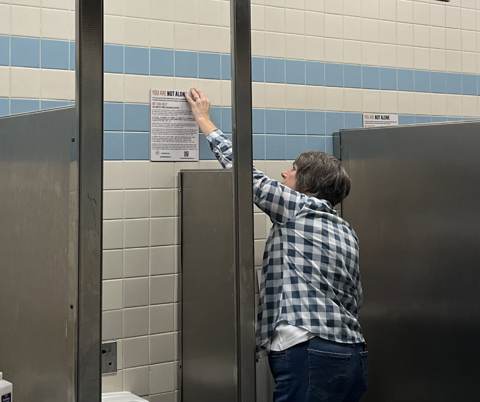 A maintenance worker installs a Not Alone sign in restroom stalls