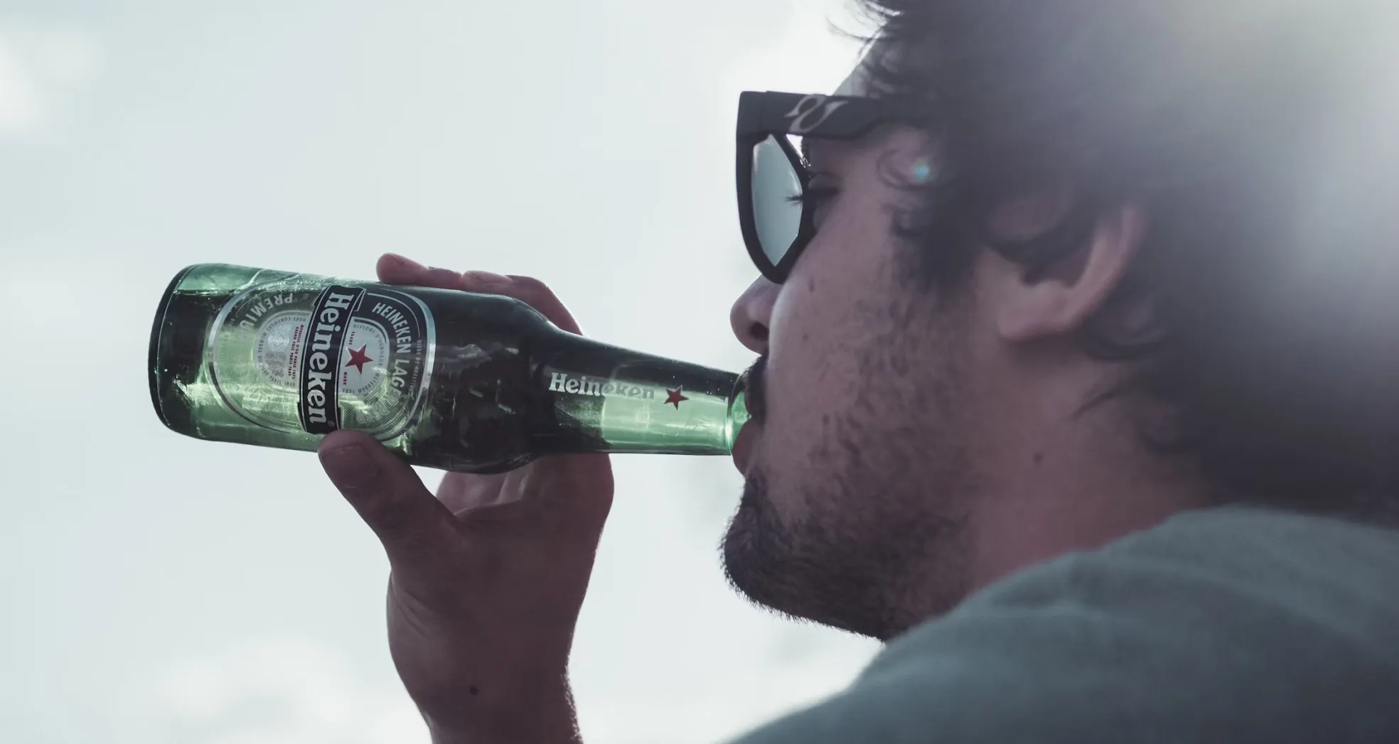 Man with sunglasses drinking from a bottle of Heineken beer